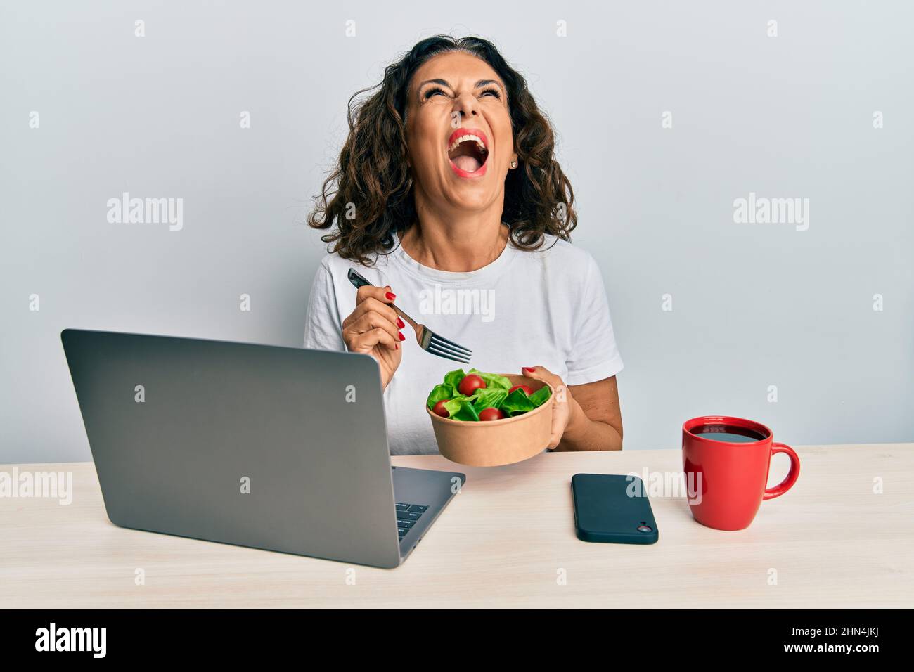 Beautiful middle age woman working at the office eating healthy salad ...