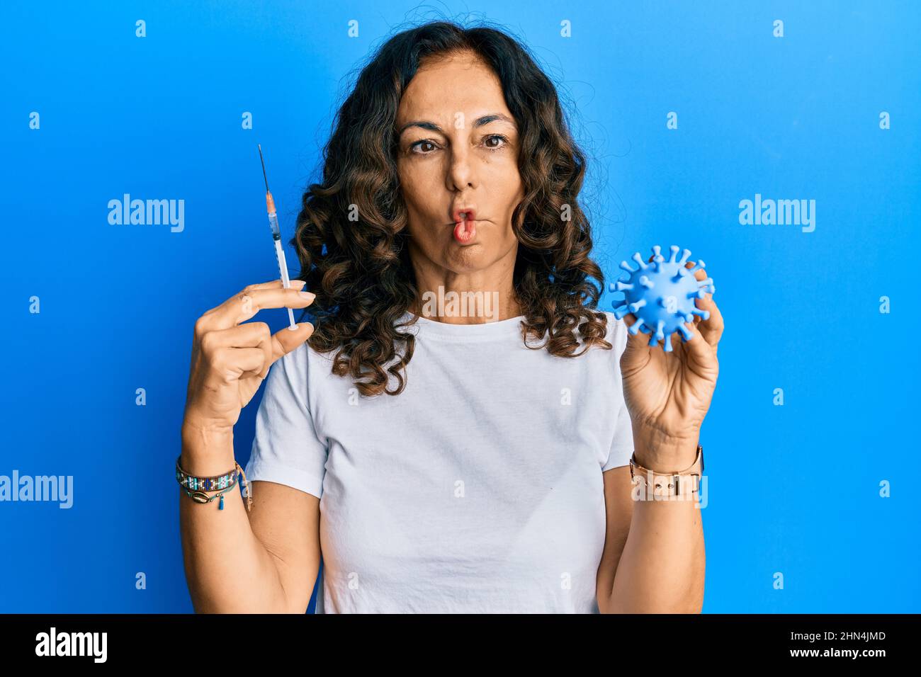 Middle age hispanic woman holding virus toy and syringe making fish ...