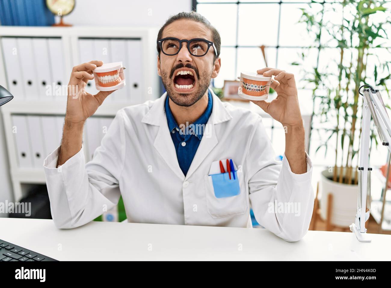Young hispanic dentist man holding denture with orthodontic braces ...