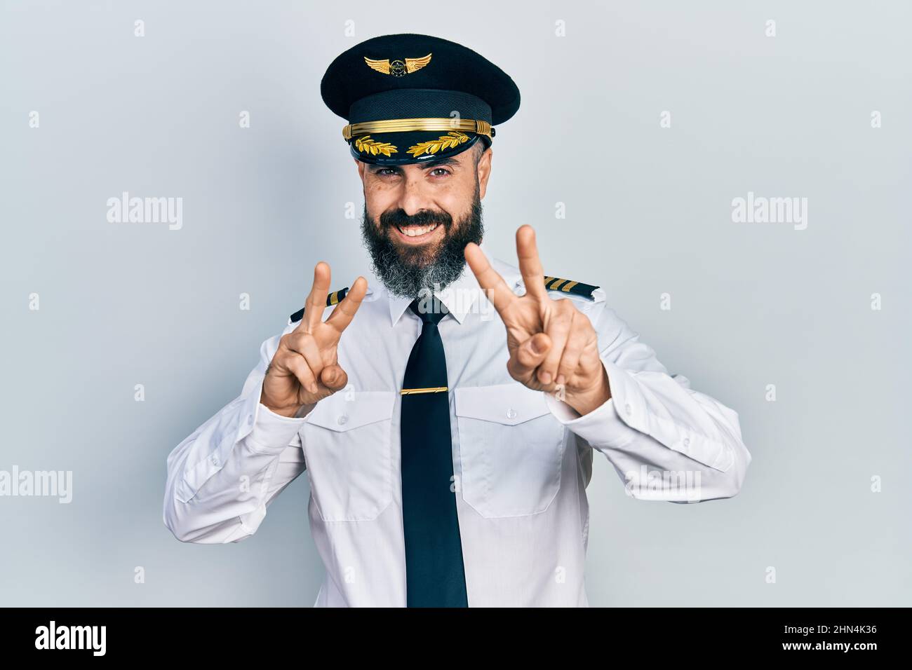 Young hispanic man wearing airplane pilot uniform smiling looking to ...