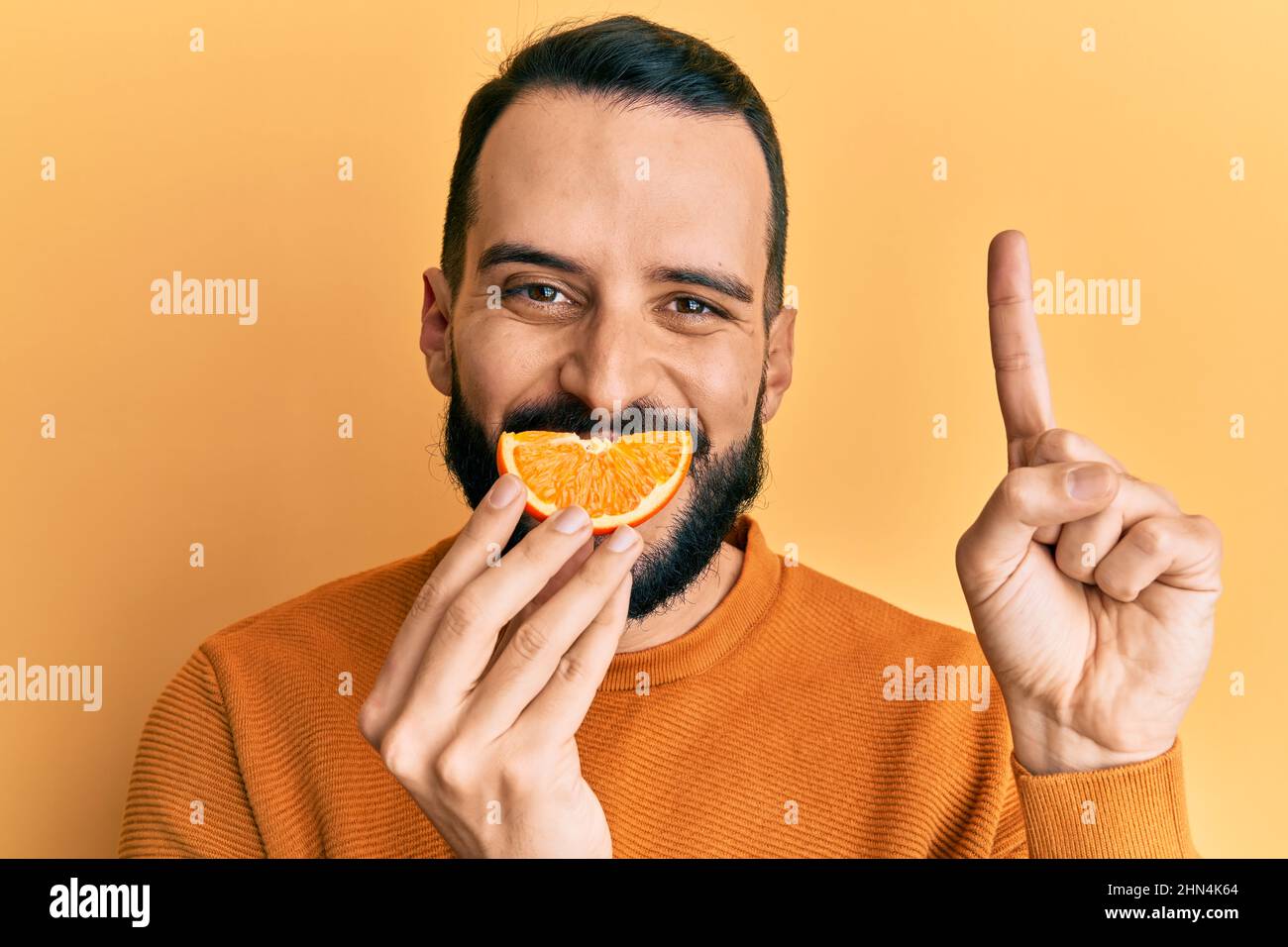 Young man with beard holding orange slice on mouth as funny smile ...
