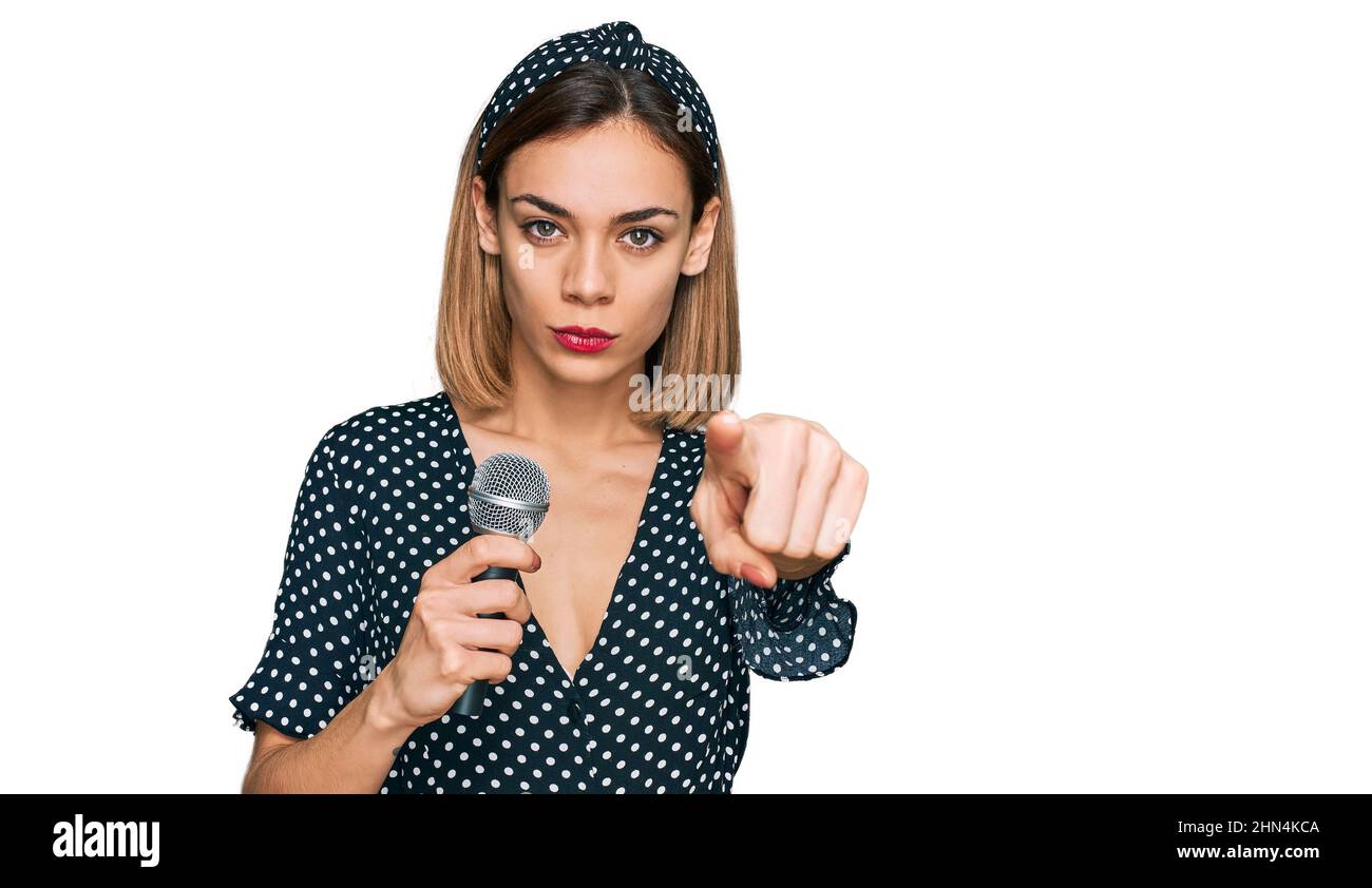 Young blonde girl singing song using microphone pointing with finger to ...