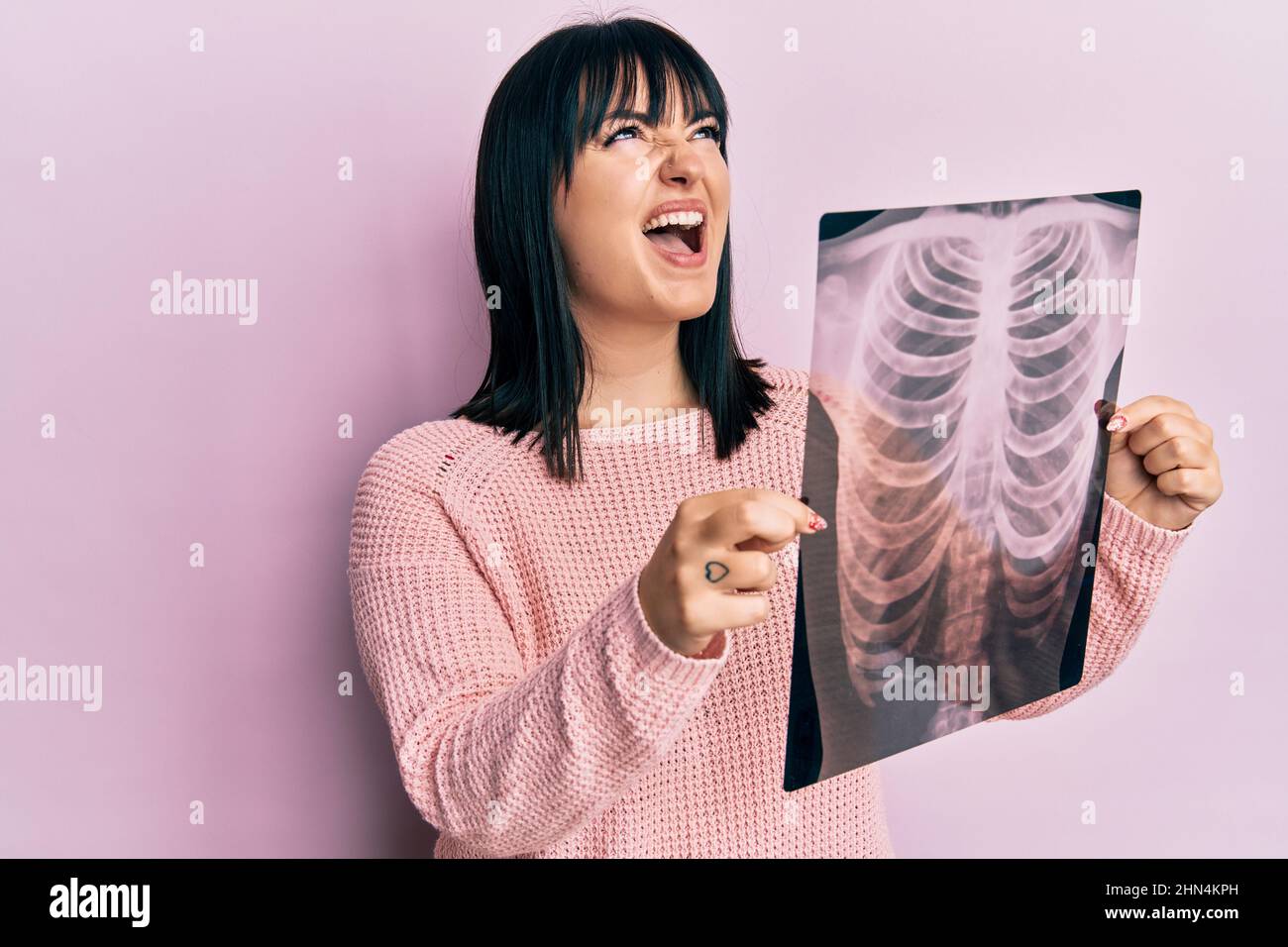 Young hispanic woman holding chest x-ray angry and mad screaming ...