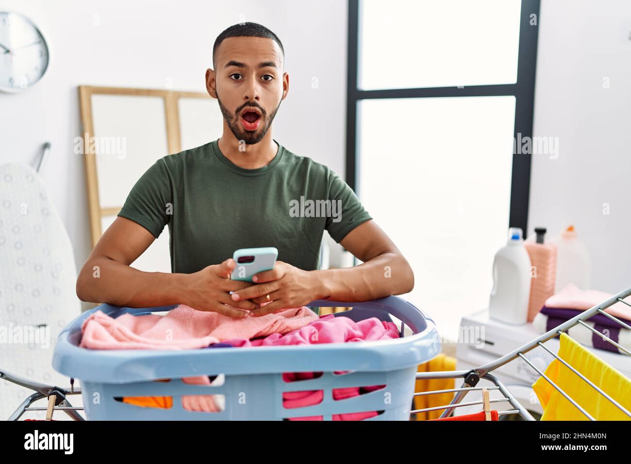 African american man doing laundry using smartphone afraid and shocked ...