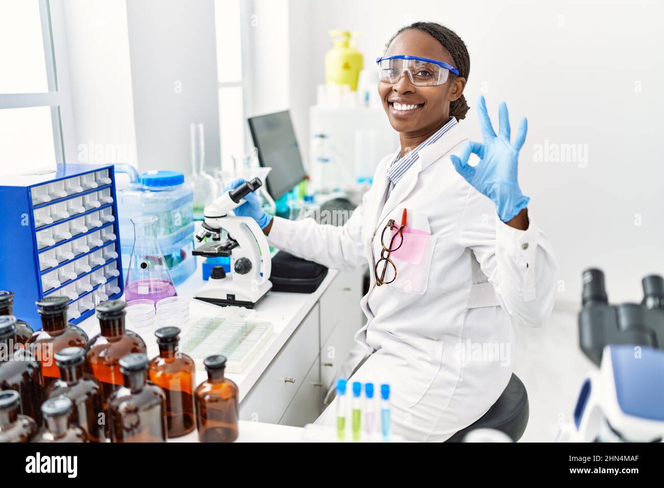 African woman working at scientist laboratory doing ok sign with ...