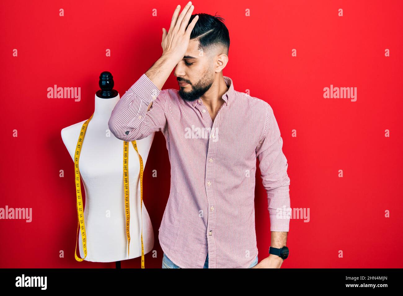 Handsome tailor man with beard standing by manikin surprised with hand ...