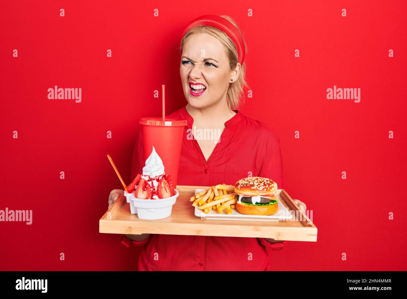 Young blonde woman eating a tasty classic burger with fries and soda ...