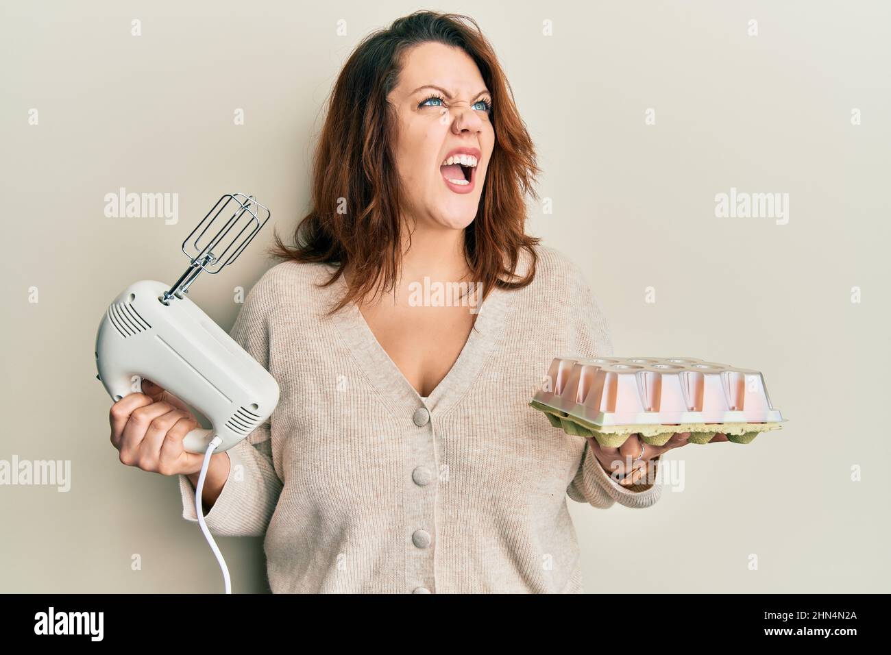 Young caucasian woman holding pastry blender electric mixer and eggs ...