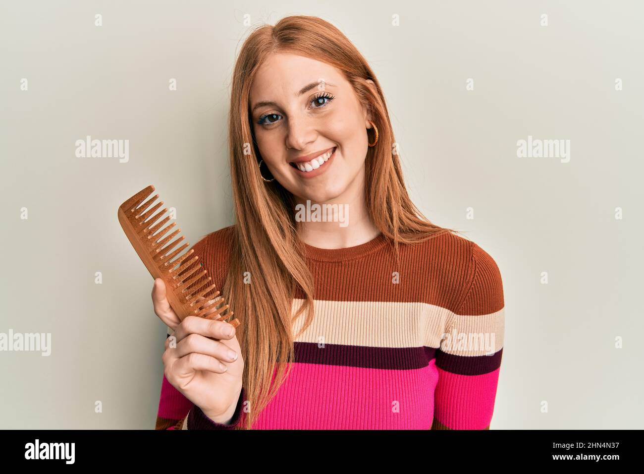 Young irish woman styling hair using comb looking positive and happy ...