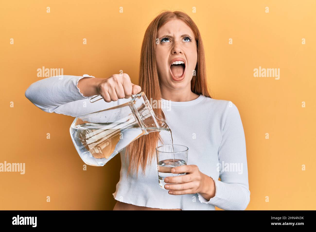 Young irish woman pouring water angry and mad screaming frustrated and ...