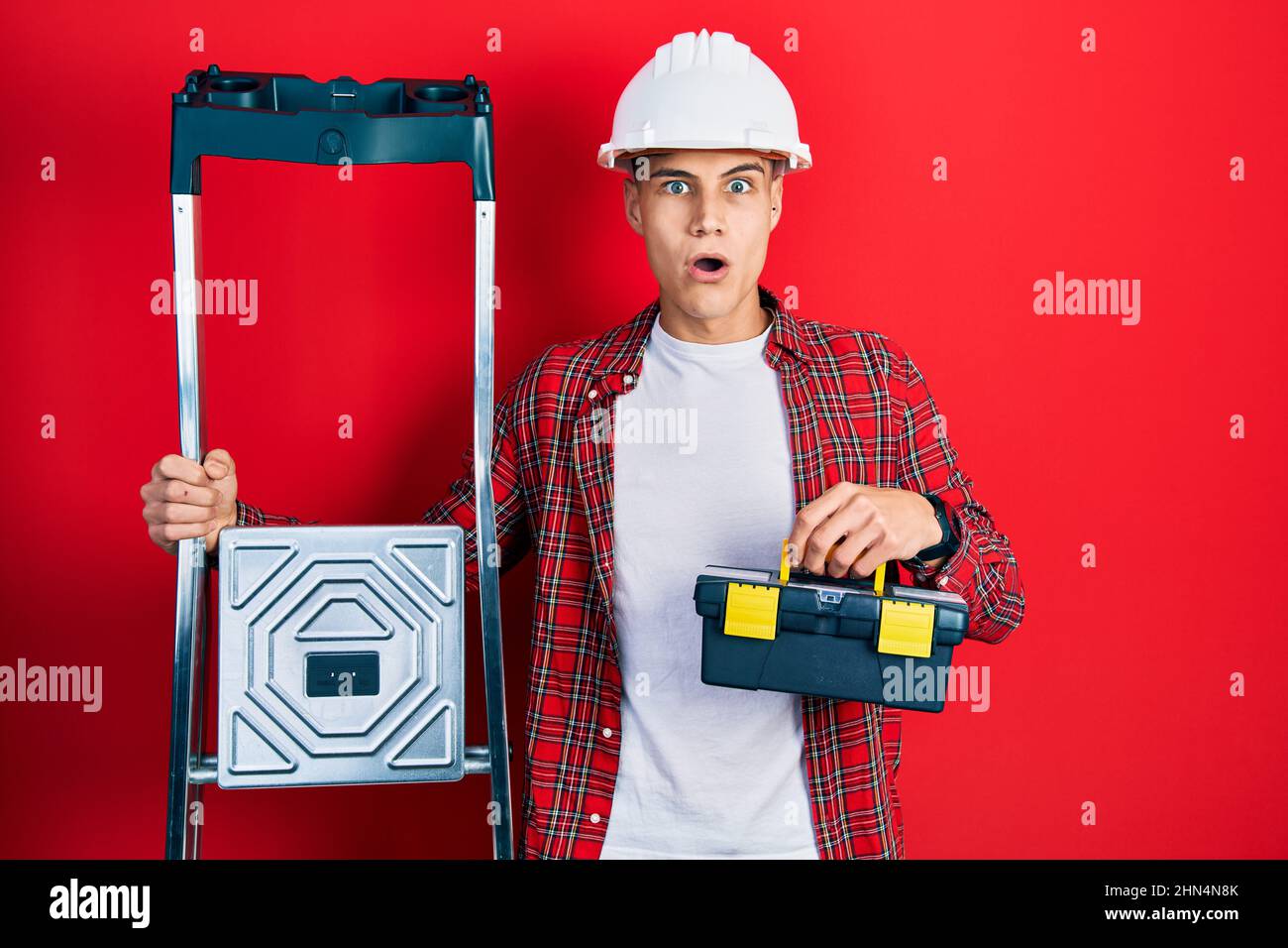 Young hispanic man holding tools box wearing hardhat by construction ...