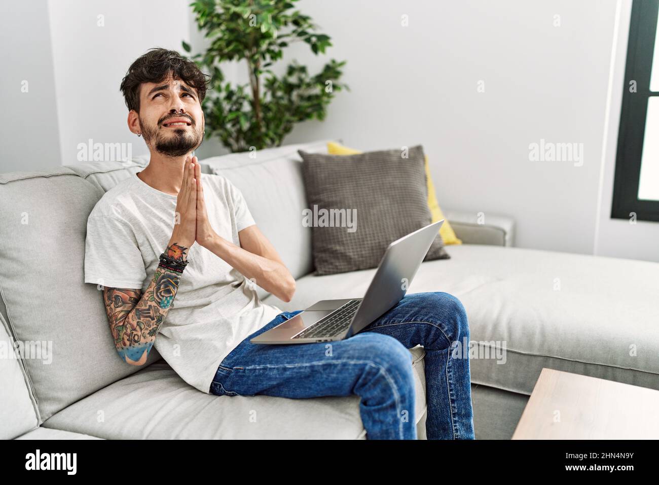 Hispanic man with beard sitting on the sofa begging and praying with ...