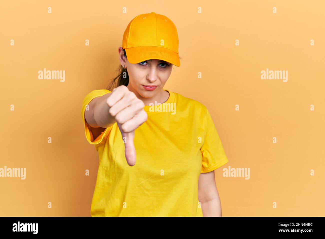 Young hispanic woman wearing delivery uniform and cap looking unhappy ...