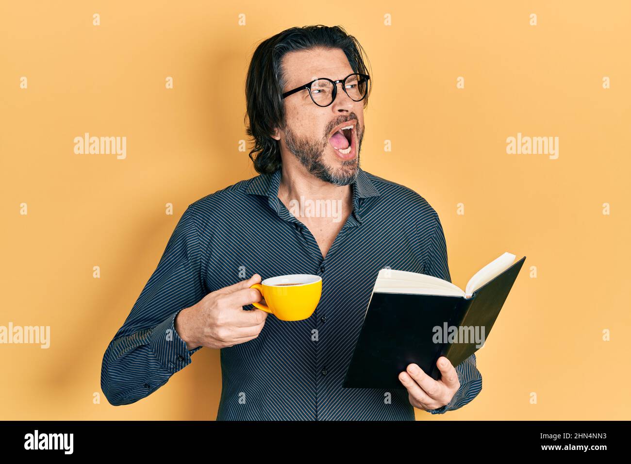 Middle age caucasian man reading book drinking cup of tea angry and mad ...