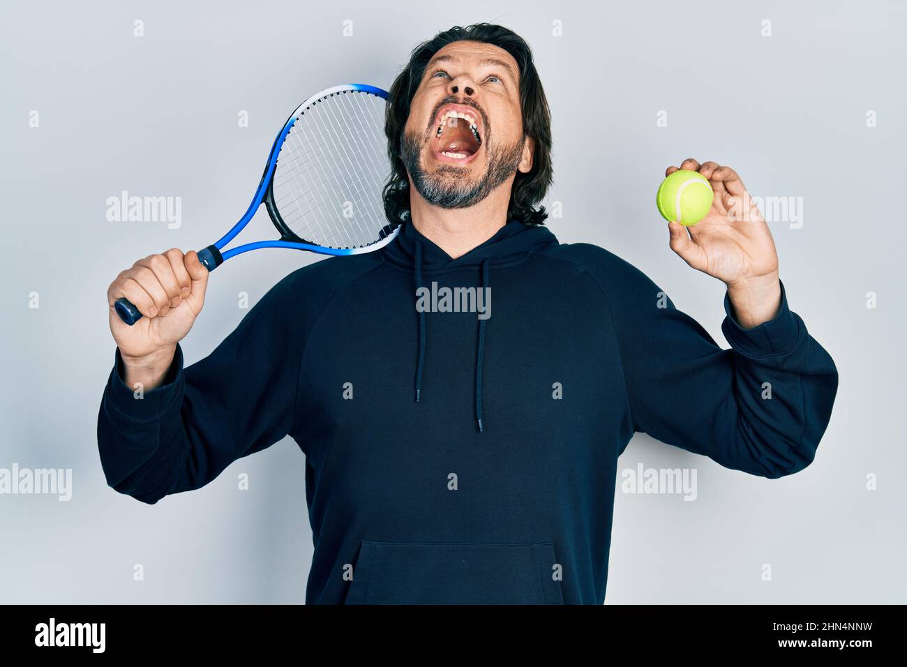 Middle age caucasian man playing tennis holding racket and ball angry ...