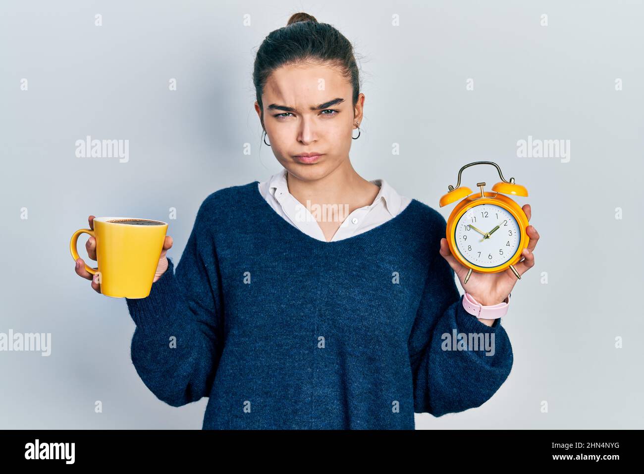 Young caucasian girl holding coffee and alarm clock skeptic and nervous ...