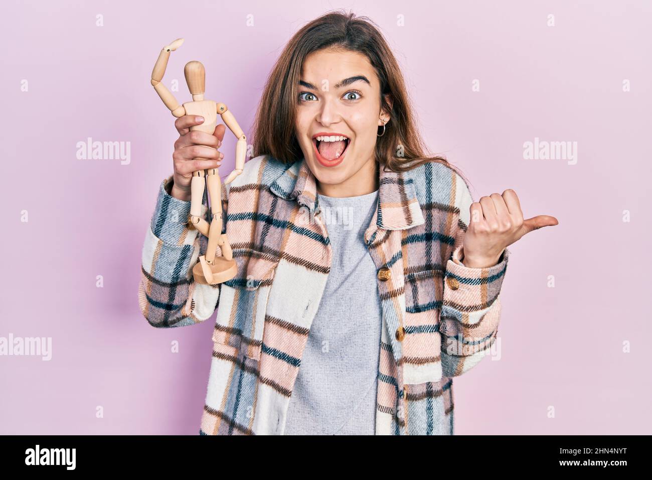 Young caucasian girl holding small wooden manikin pointing thumb up to ...