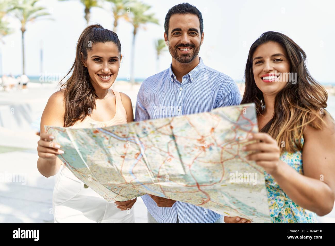 Three young hispanic friends smiling happy searching route on city map ...