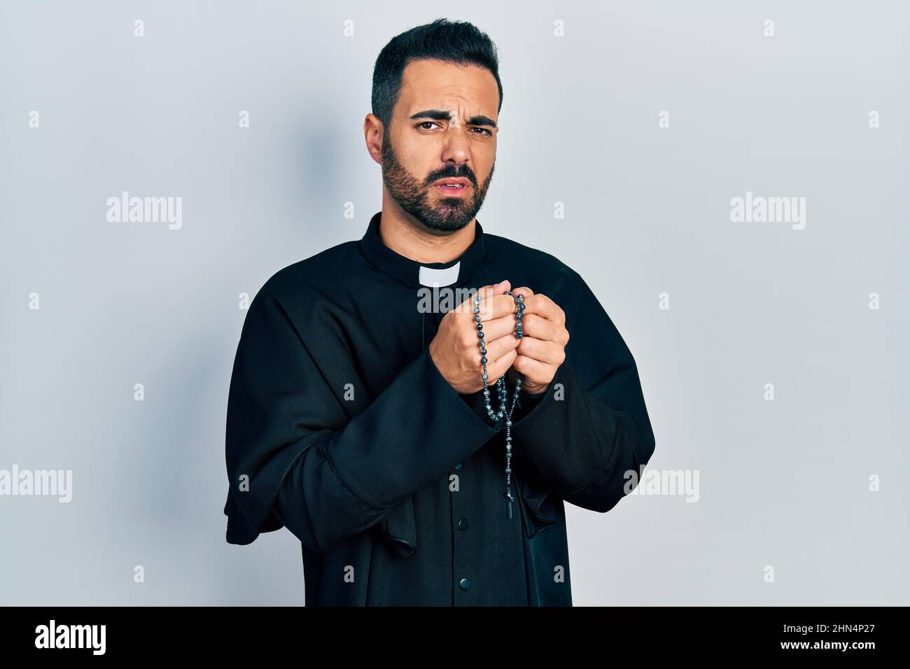 Handsome hispanic priest man with beard praying holding catholic rosary ...