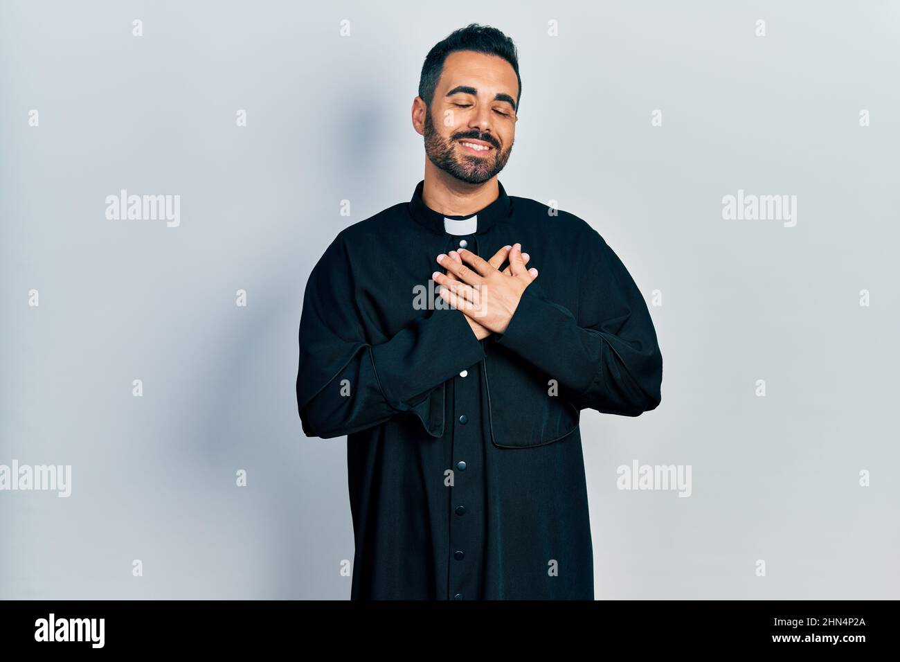 Handsome hispanic man with beard wearing catholic priest robe smiling ...