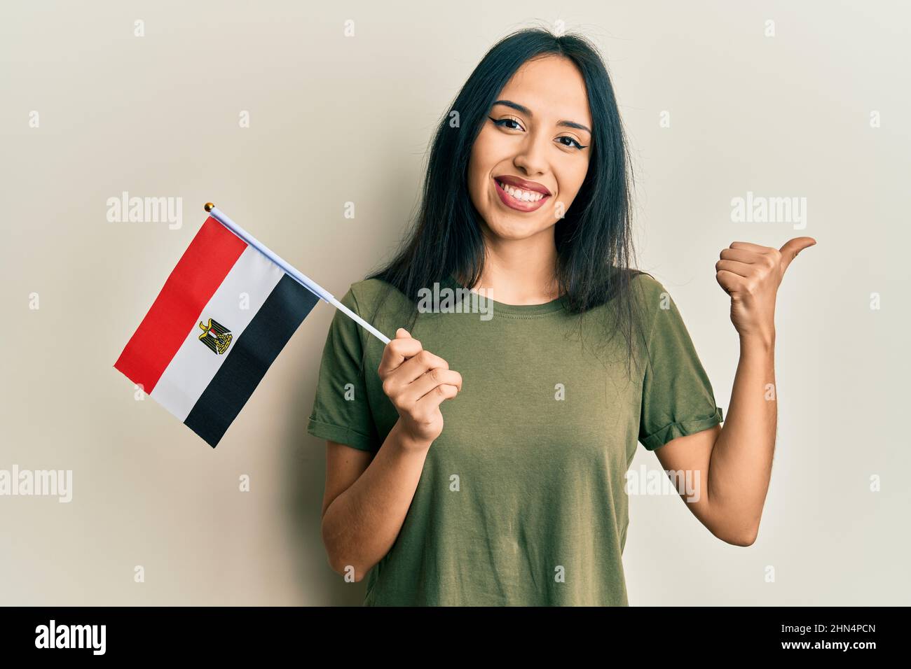 Young hispanic girl holding egypt flag pointing thumb up to the side ...