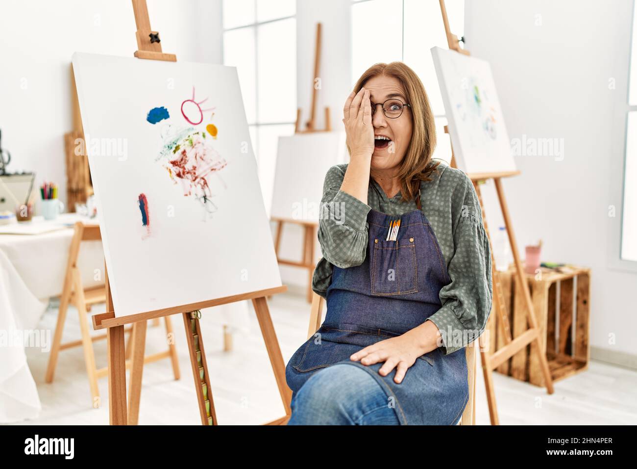 Middle age artist woman at art studio covering one eye with hand ...