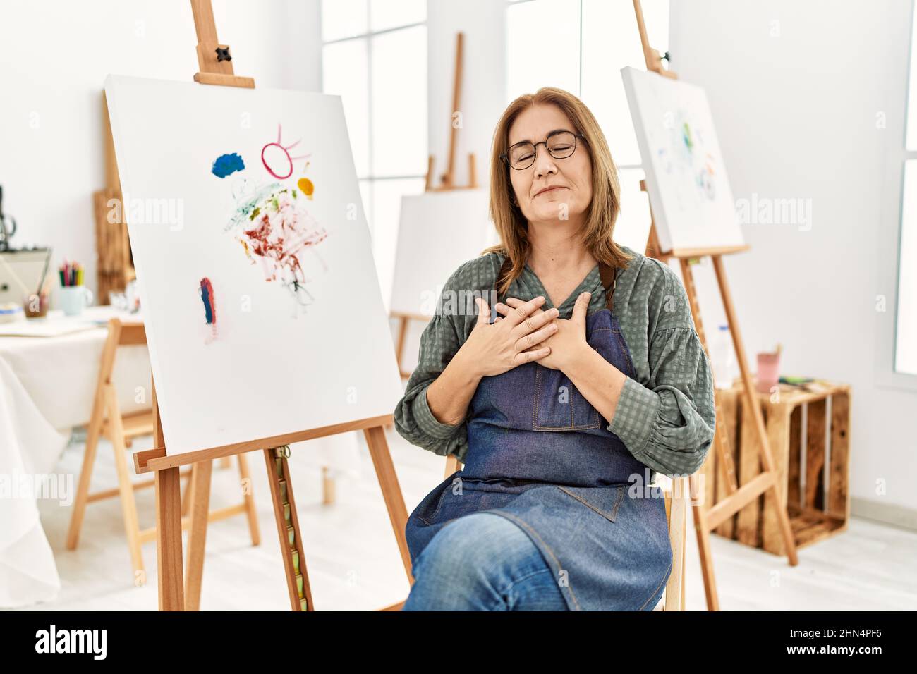 Middle age artist woman at art studio smiling with hands on chest with ...