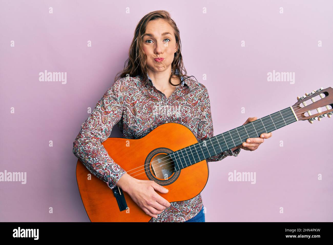 Young blonde woman playing classical guitar puffing cheeks with funny ...