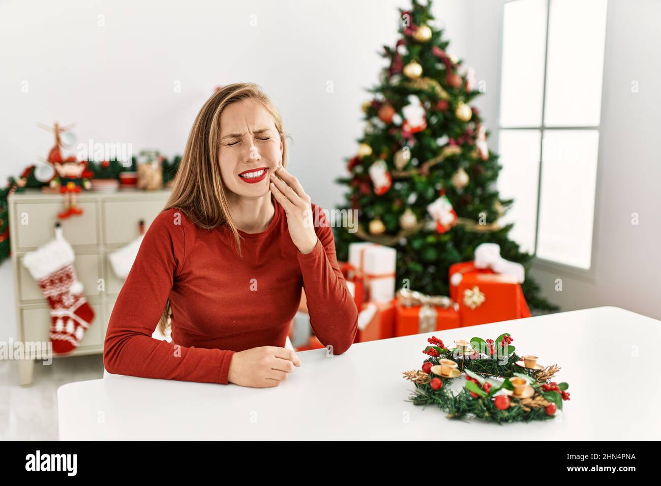 Caucasian young blonde woman sitting on the table by christmas tree ...