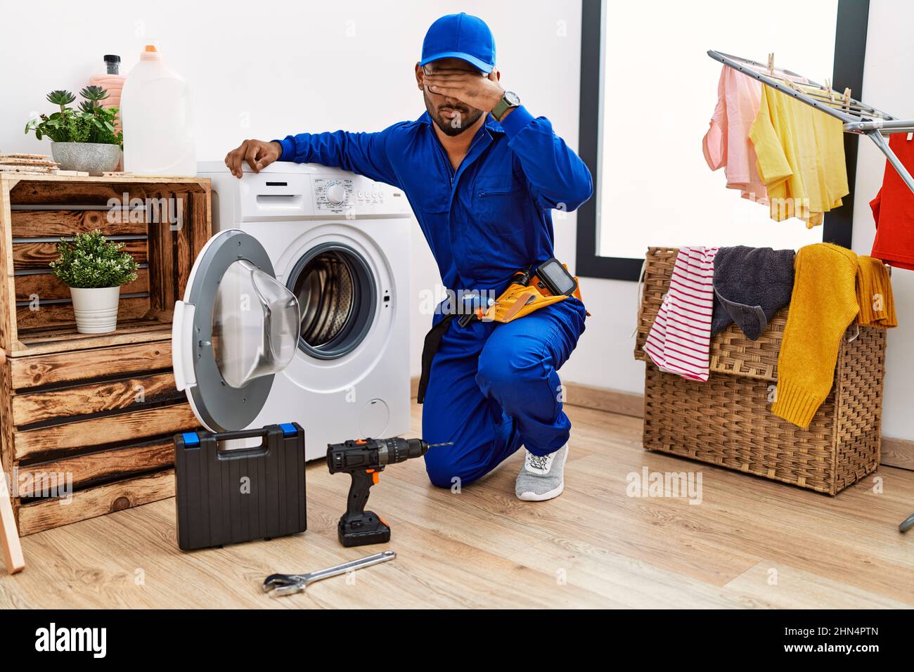 Young indian technician working on washing machine covering eyes with ...