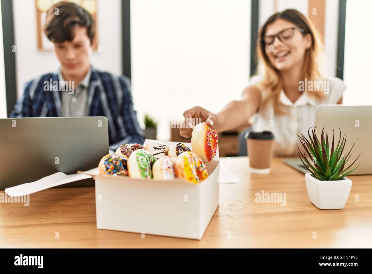 Two business workers smiling happy eating doughnuts at the office Stock ...