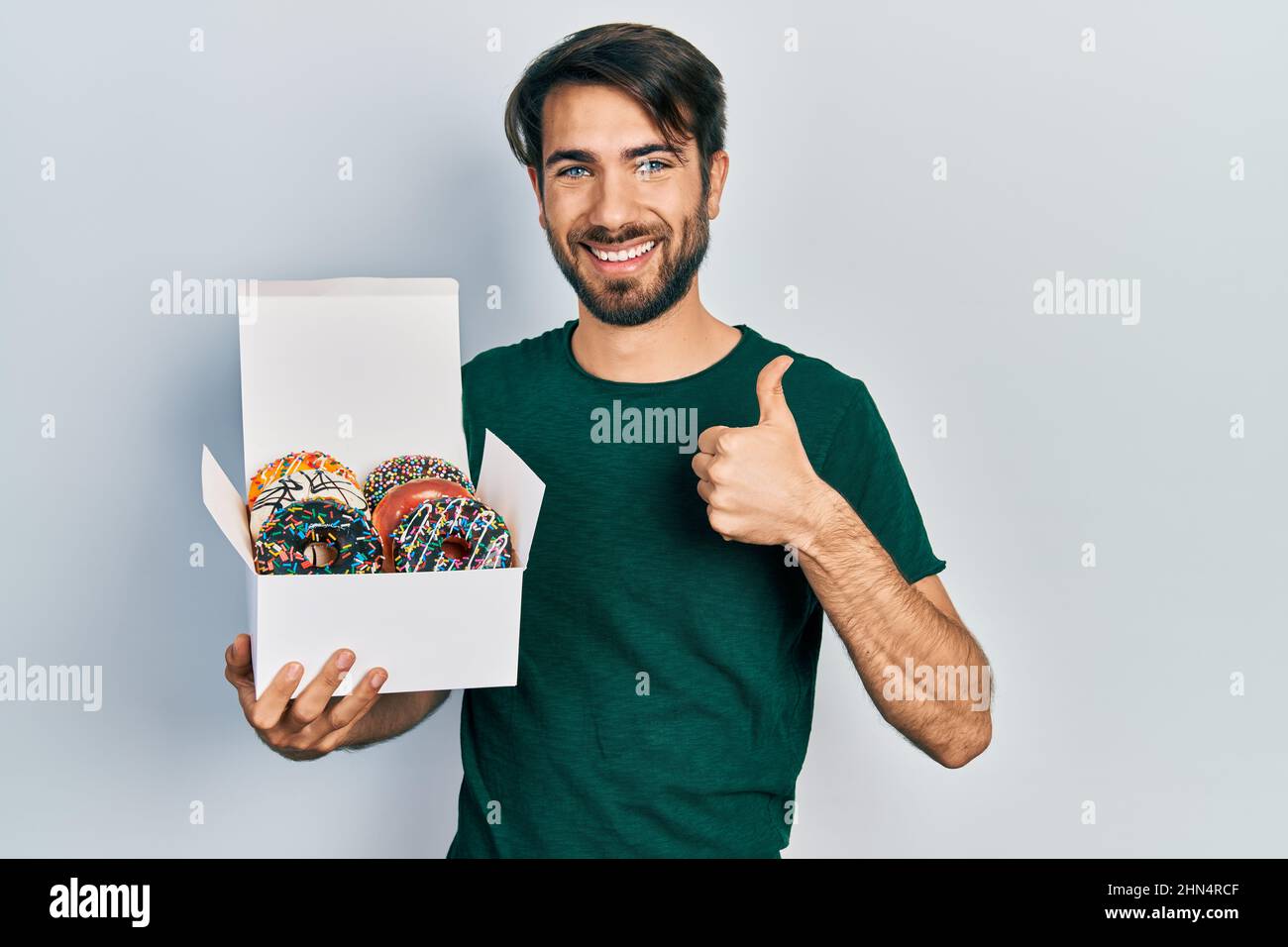 Young hispanic man holding box of tasty colorful doughnuts smiling ...