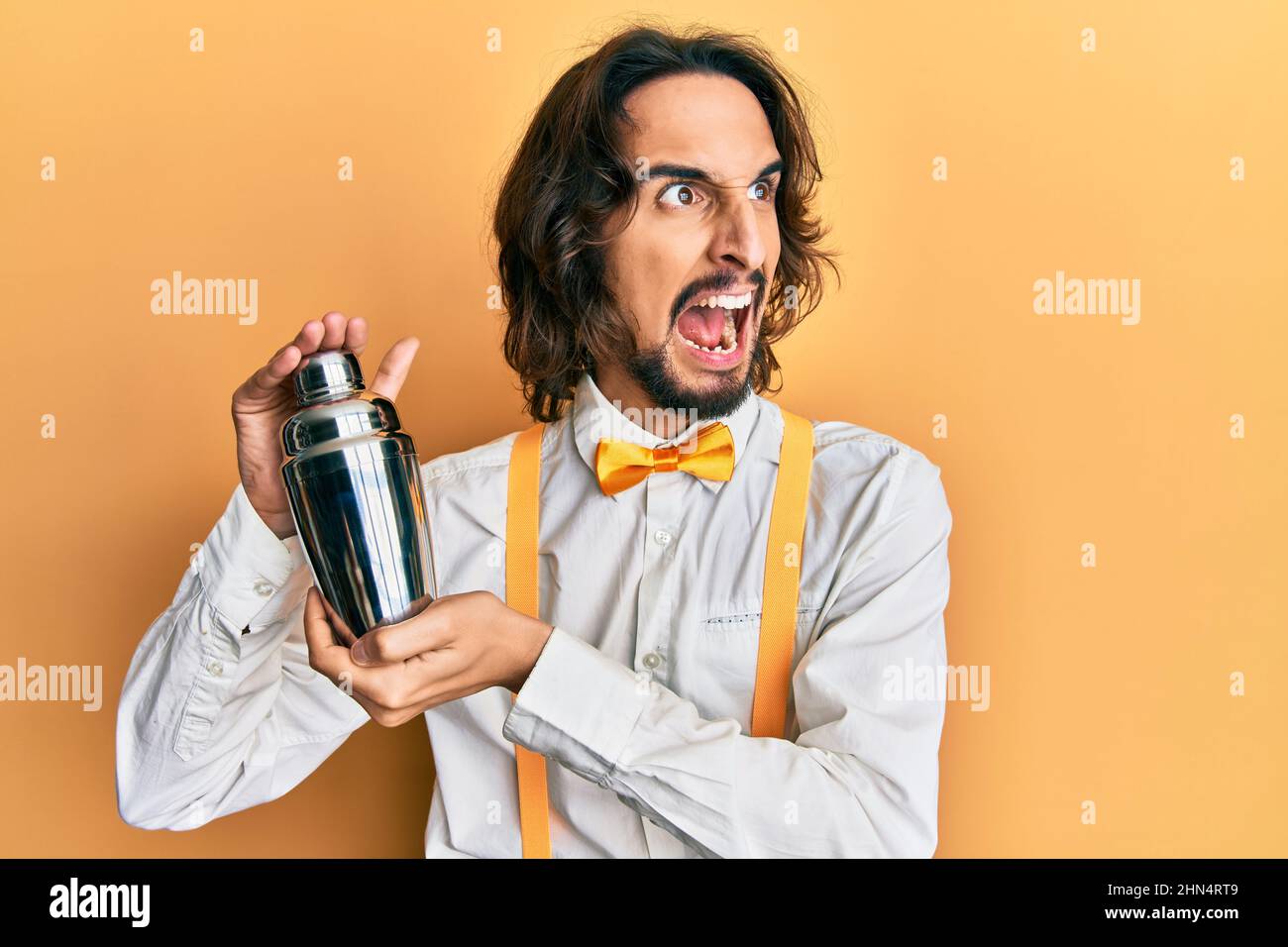 Young hispanic man preparing cocktail mixing drink with shaker angry ...