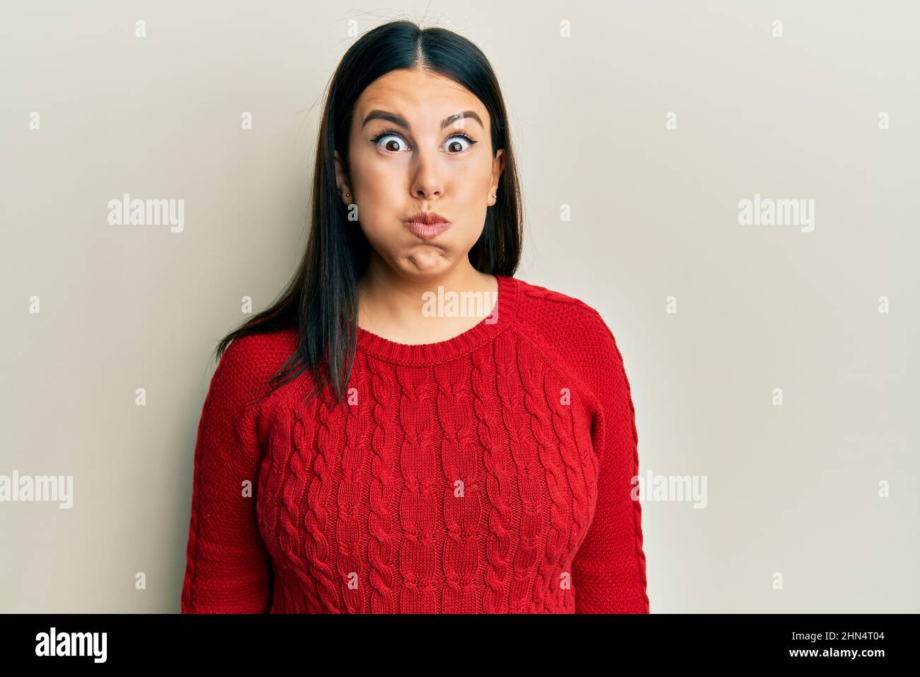 Beautiful brunette woman wearing wool winter sweater puffing cheeks ...