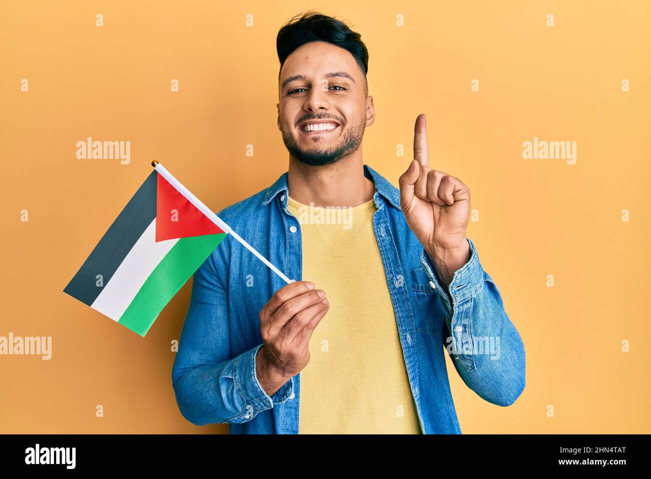 Young arab man holding palestine flag smiling with an idea or question ...