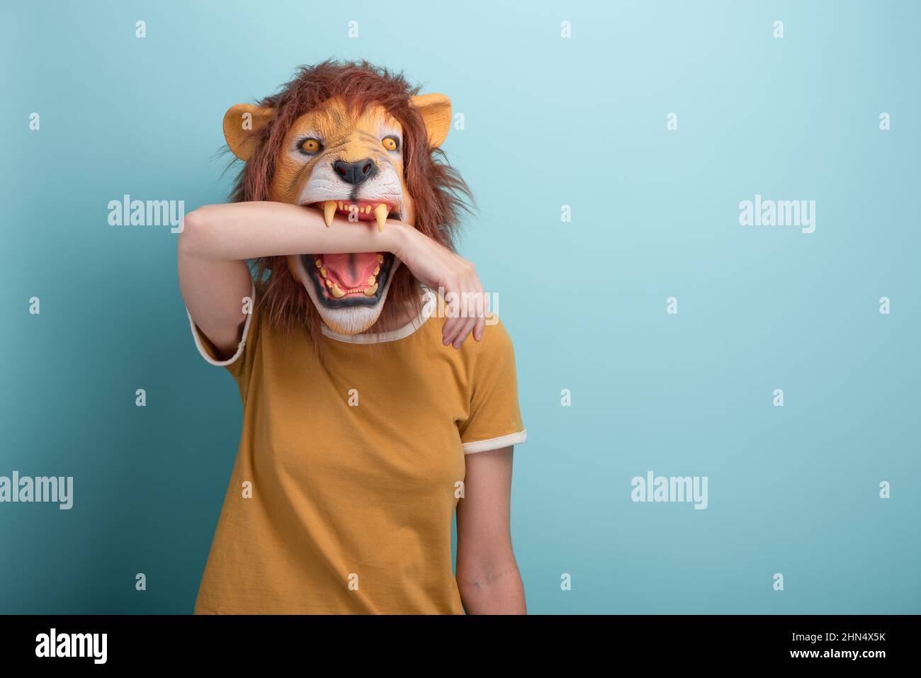 Young woman in lion mask bite her own hand, isolated on blue background ...