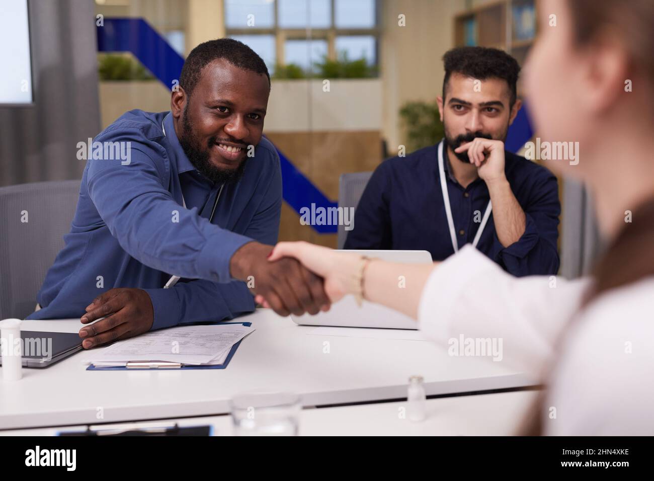 Happy young African-American businessman shaking hand of female expert ...