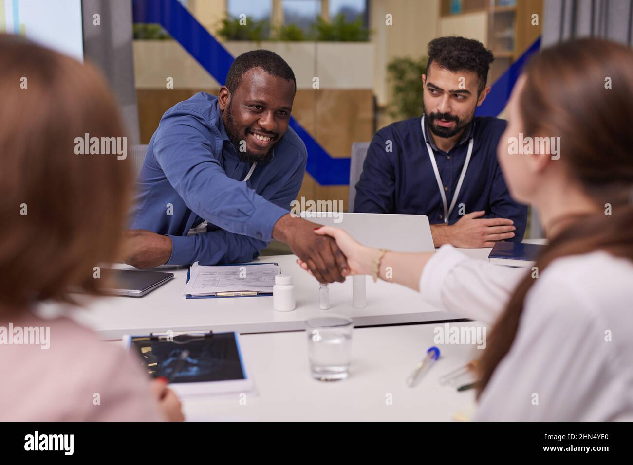 Young cheerful businessman greeting female colleague by handshake after ...