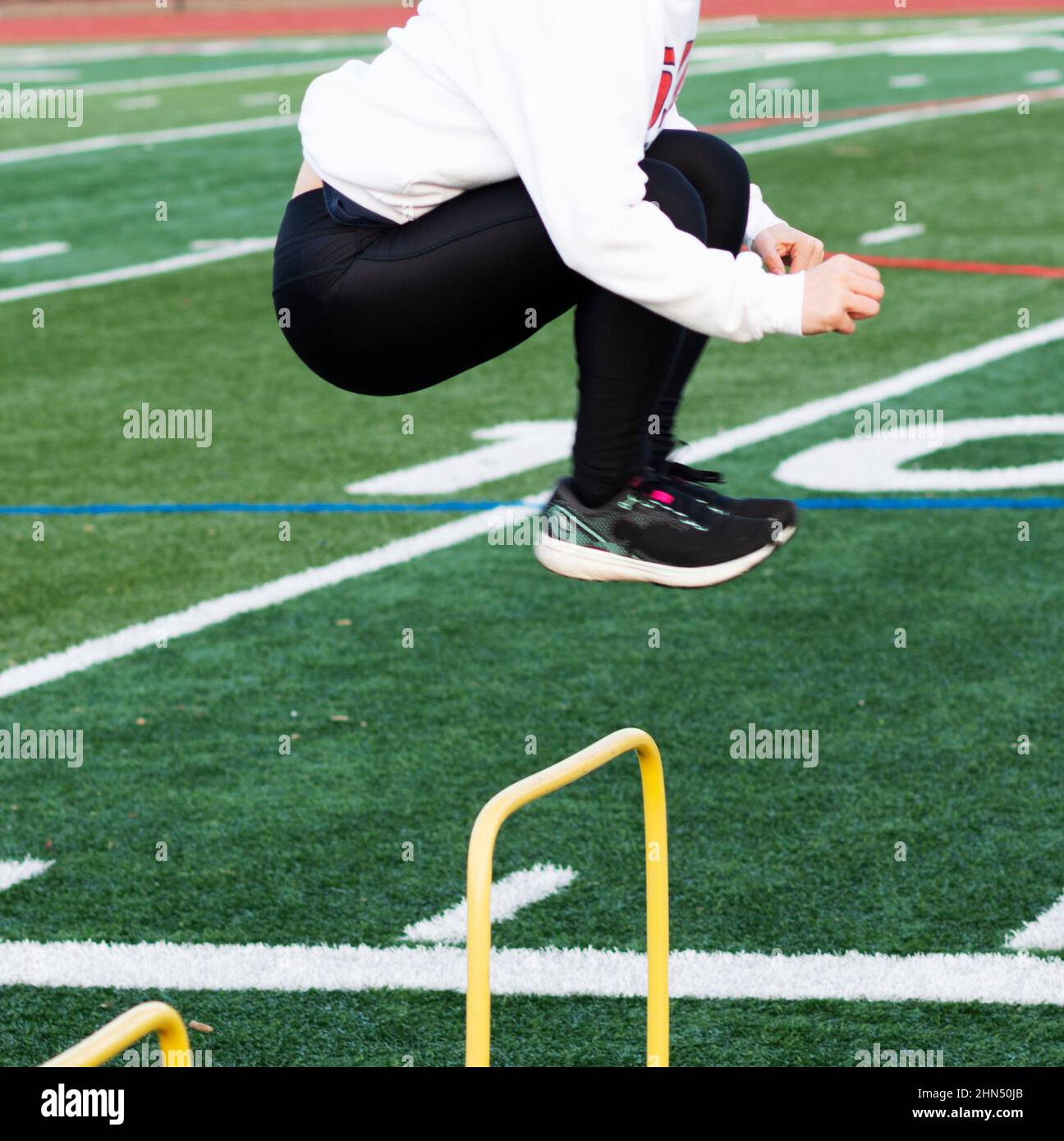 High school track and field runner jumping over a plastic yellow hurdle ...