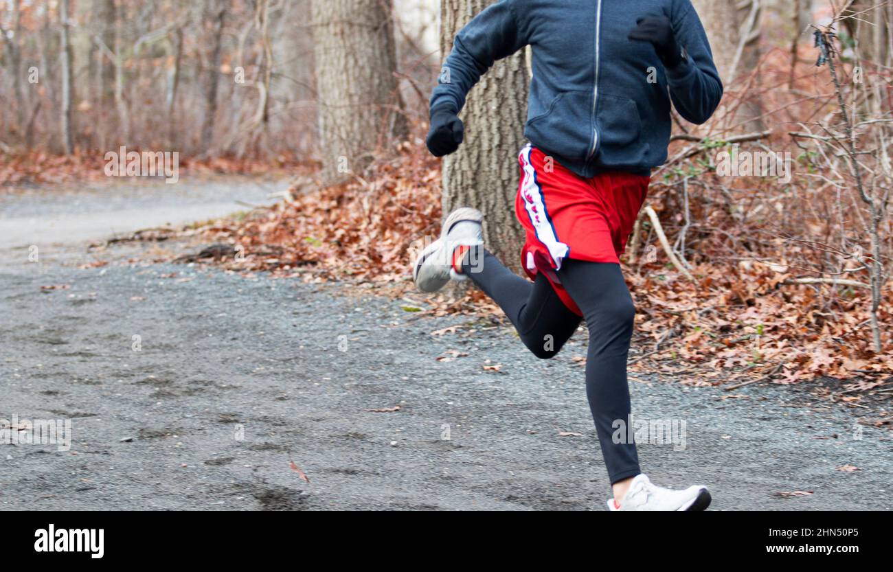 A high school boy is running on a dirt path in the woods on a small ...