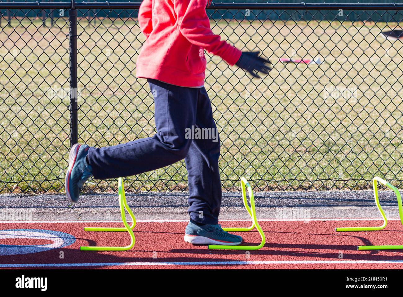 A high school track and field runner running over yellow mini hurdles on a track during practice ...