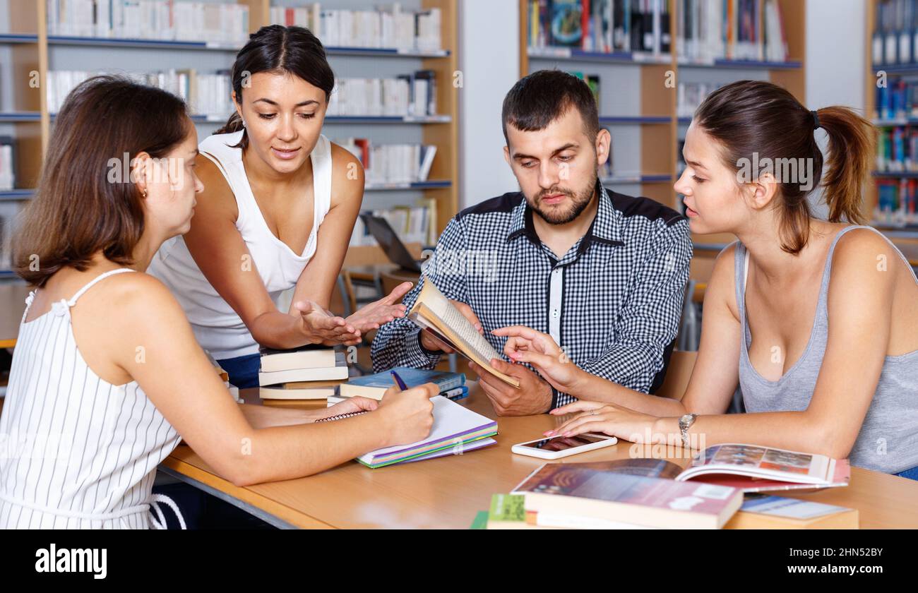 Friendly group of young students studying in university library with ...