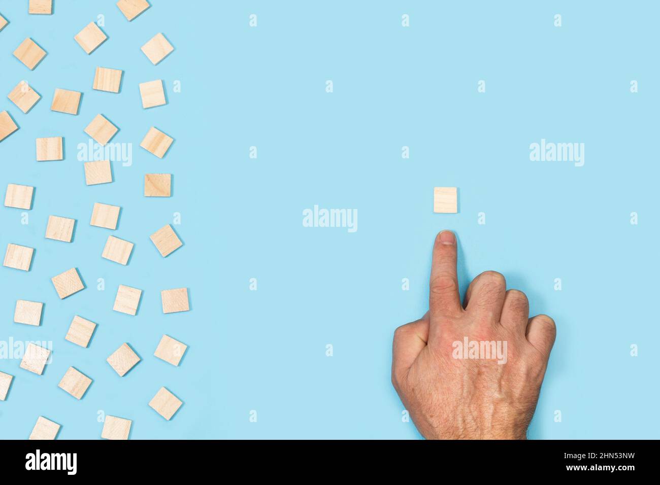 Man hand pointing a single square wooden block on a light blue ...