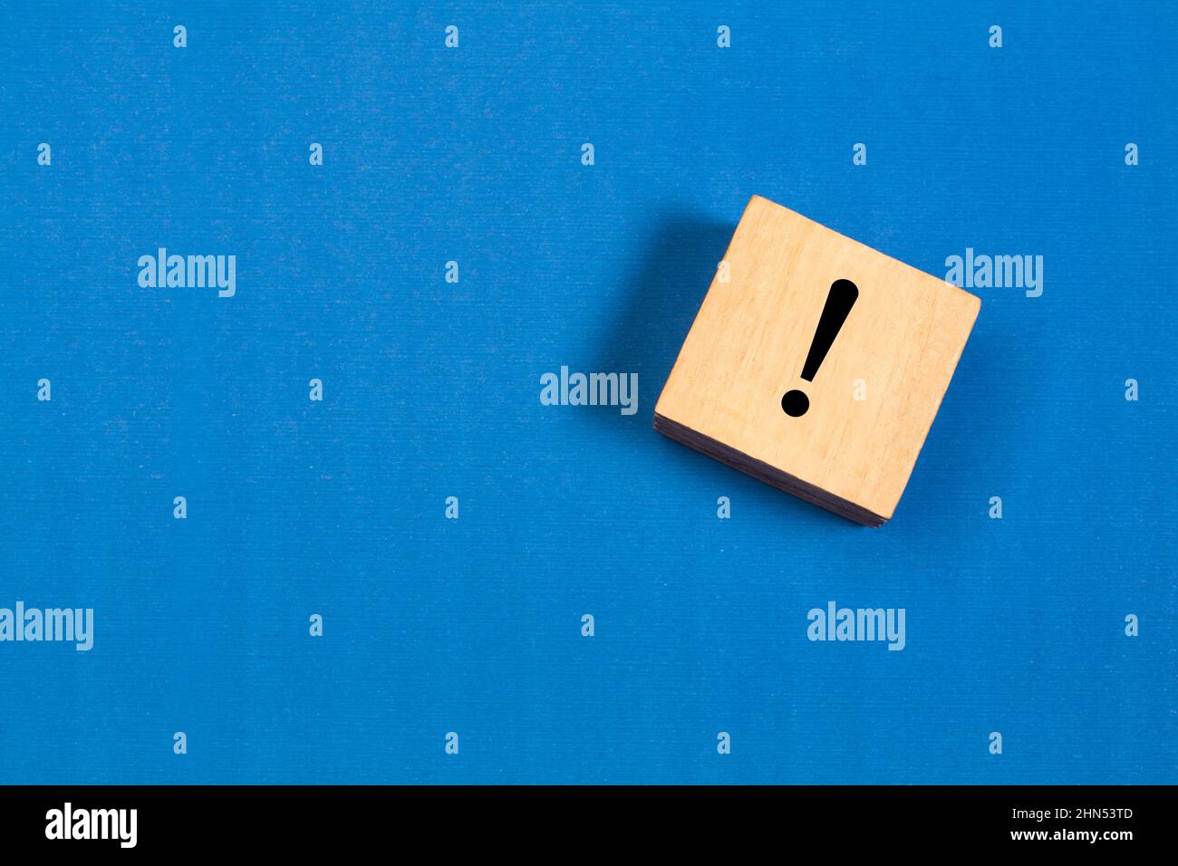 Exclamation mark sign on a wooden block on a blue background with copy ...