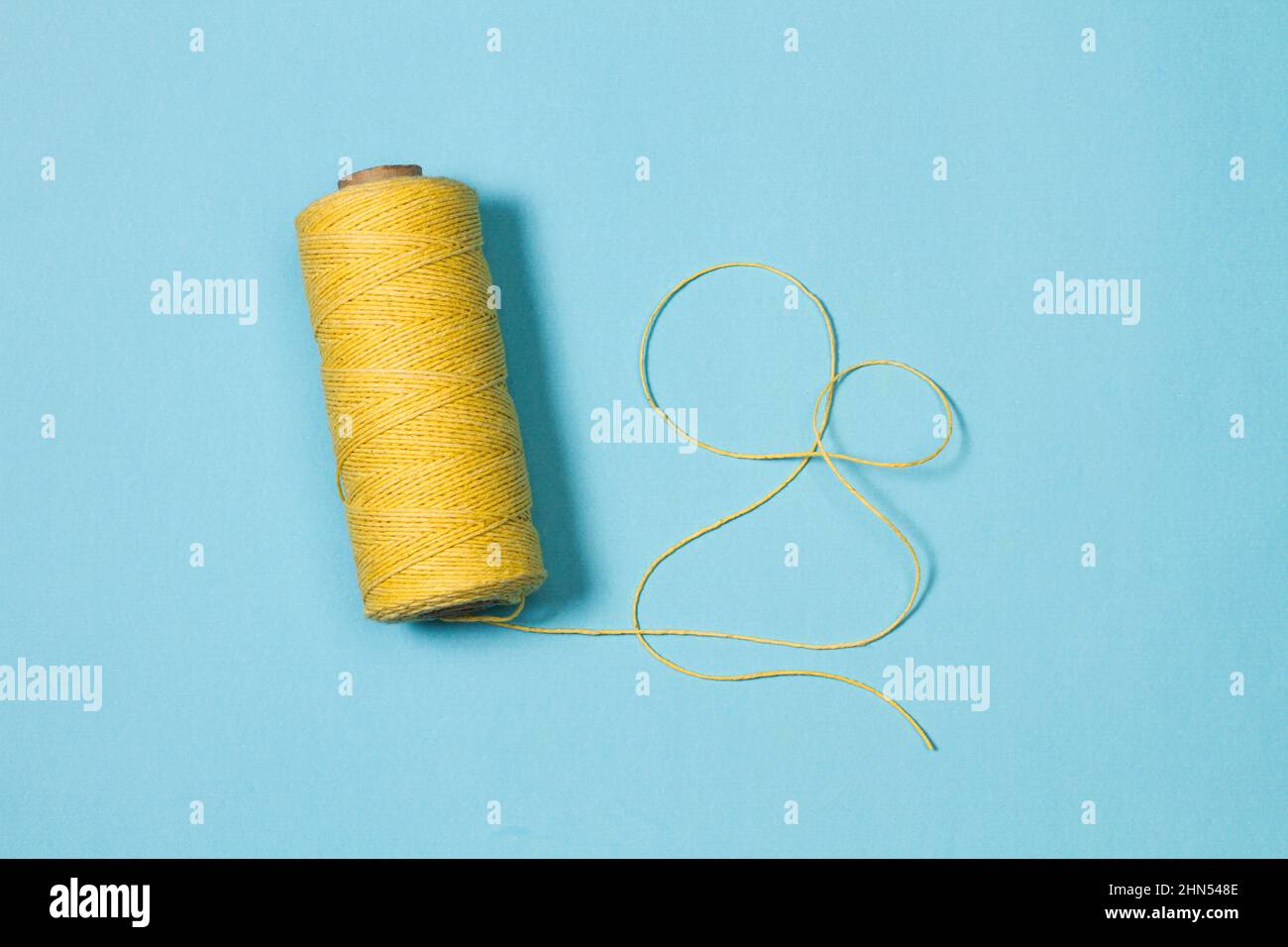 Sewing yellow thread spool on a light blue background Stock Photo - Alamy