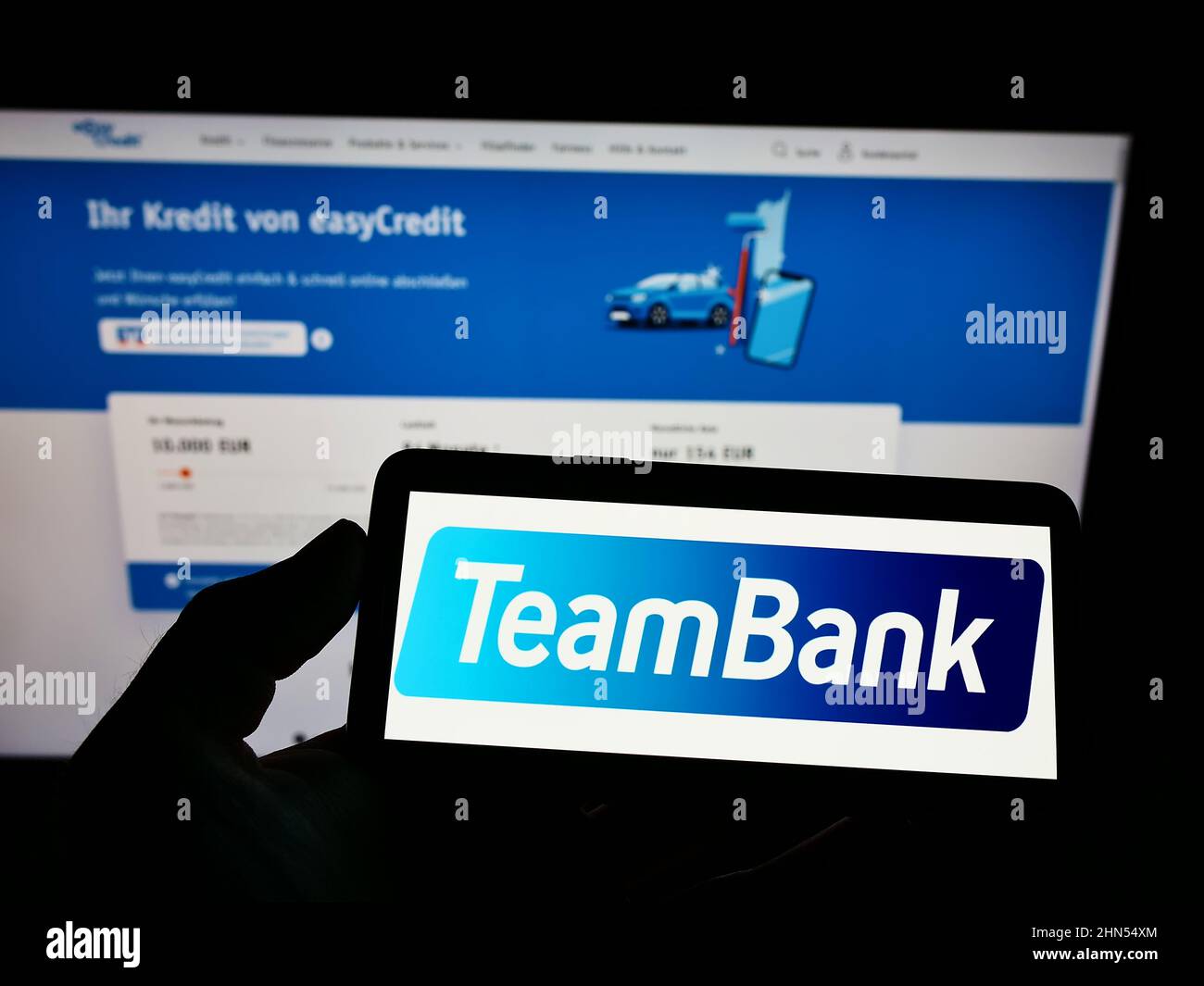 Person holding smartphone with logo of German company TeamBank AG ...