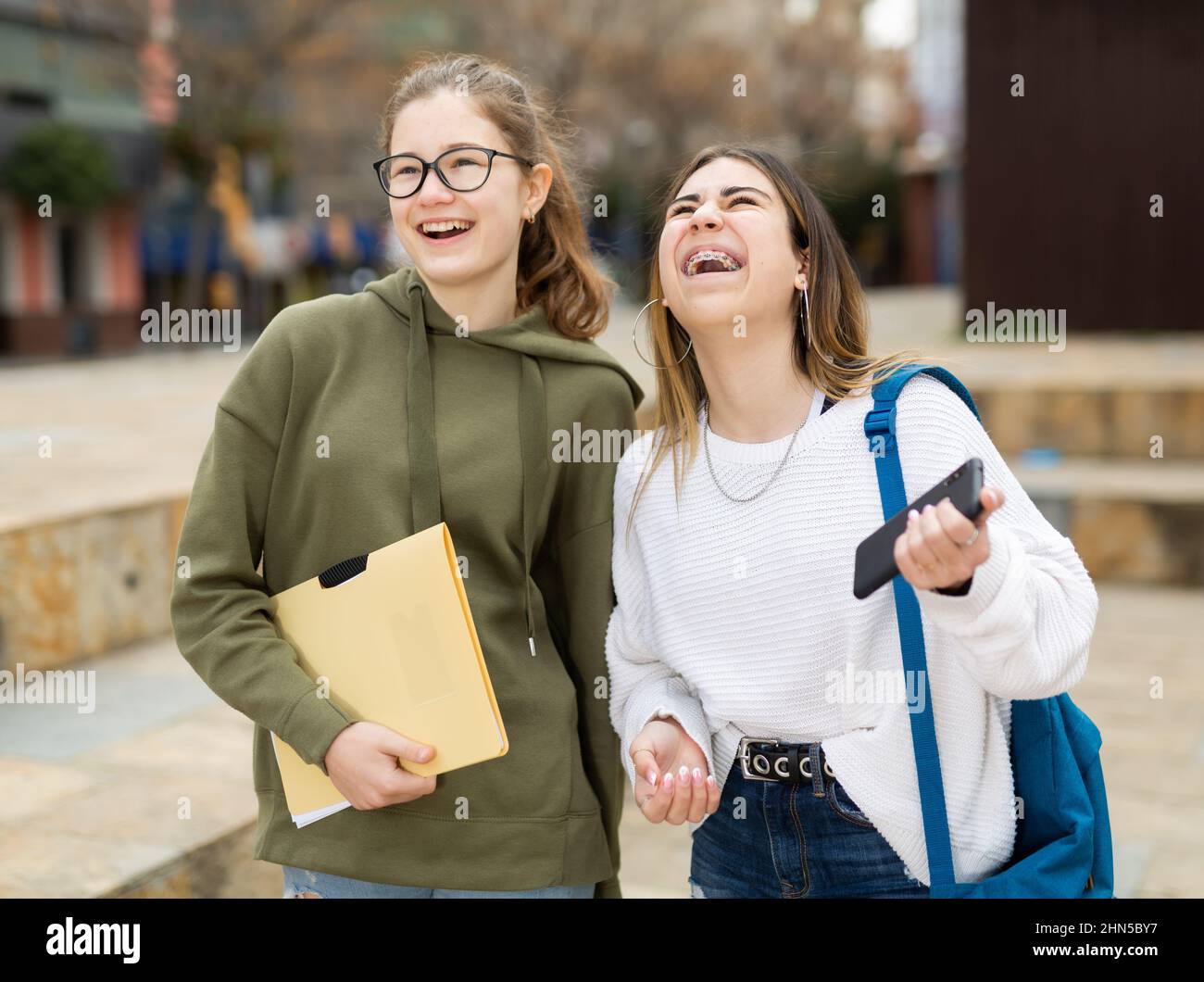 Two cheerful carefree female students walking down street Stock Photo ...