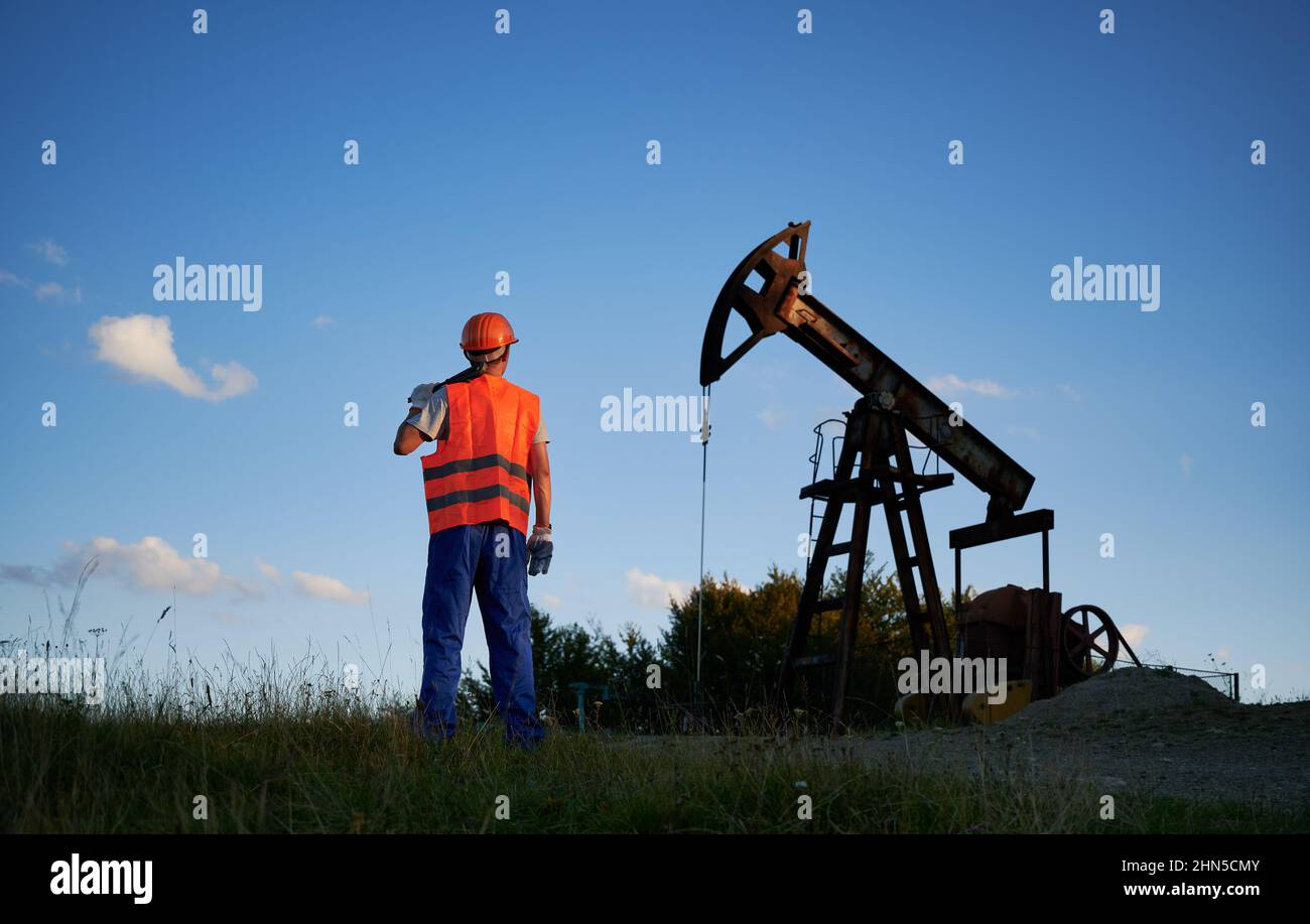 Rear view of oilman in orange uniform with working tool who watching at ...