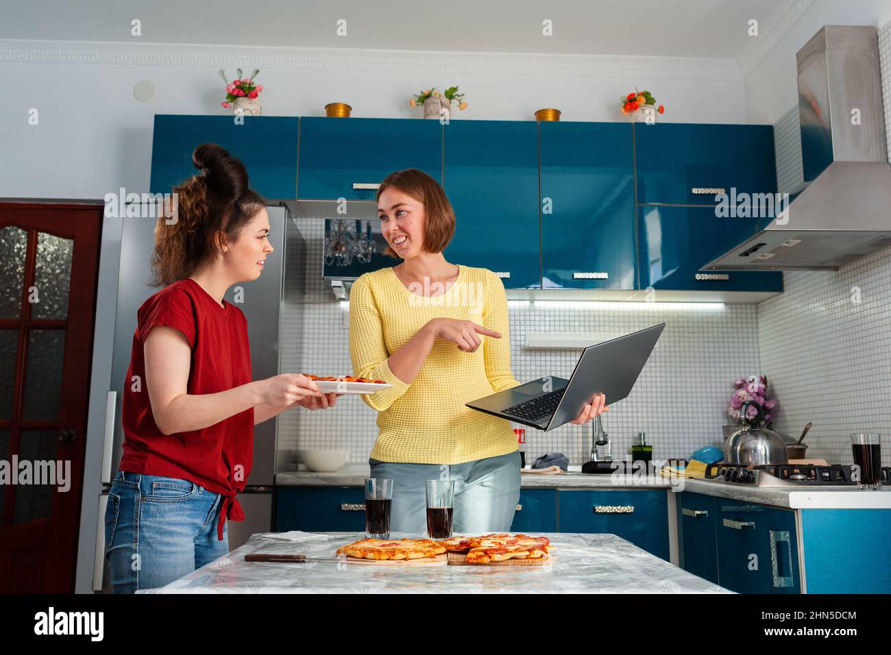 Two young women baked pizza and look at pictures with recipes on the ...