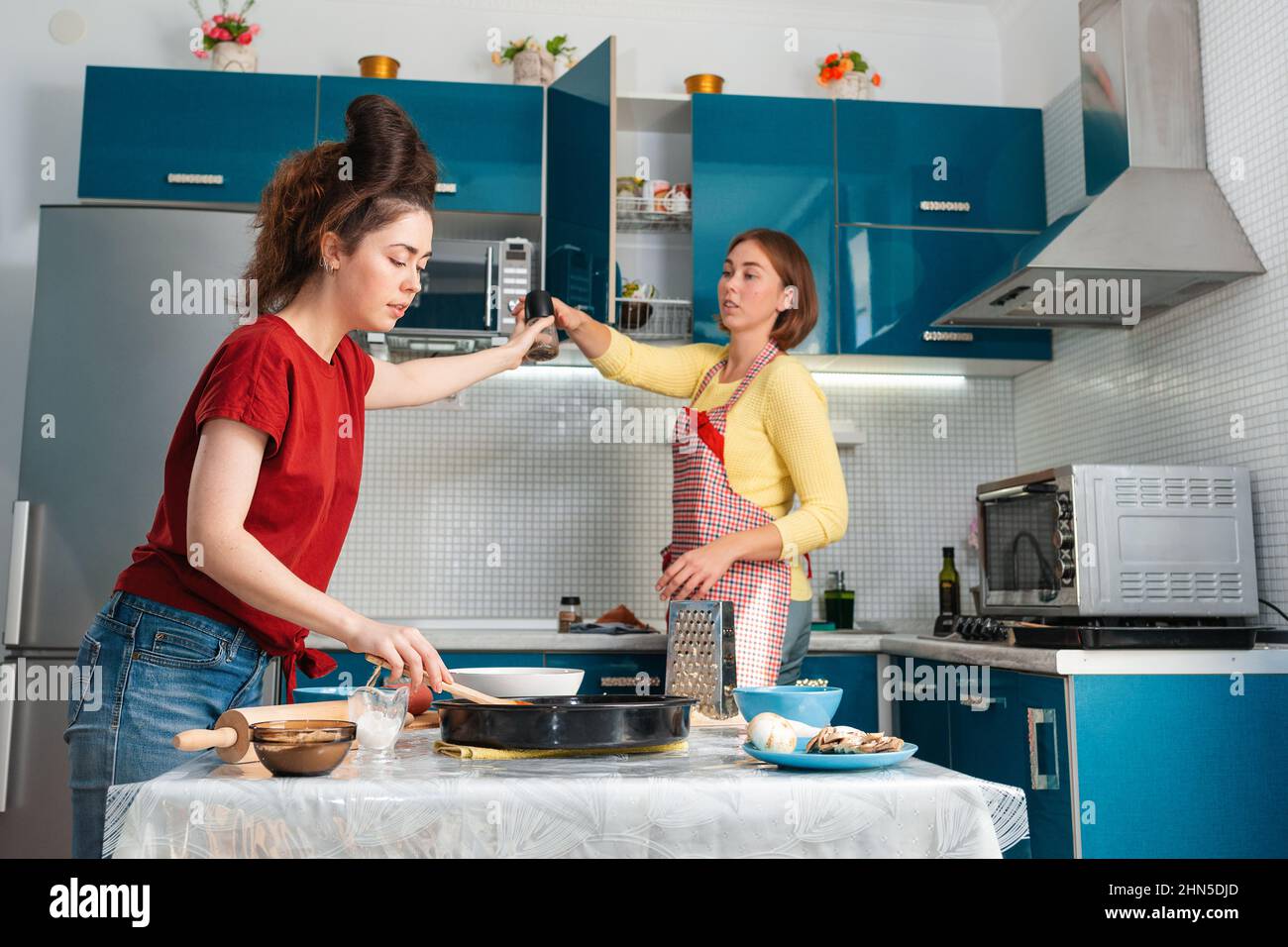 Two young pretty women prepare food together in the kitchen. The ...